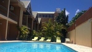 Piscina com água azul cristalina, rodeada por espreguiçadeiras e palmeiras, com um edifício ao fundo.