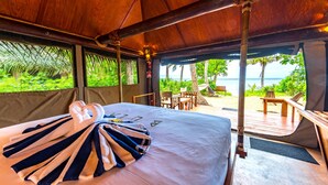 Quarto com cama, vista para a praia e deck de madeira.