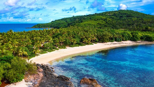 Uma praia tropical com águas turquesa cristalinas, areal arenoso e vegetação densa.