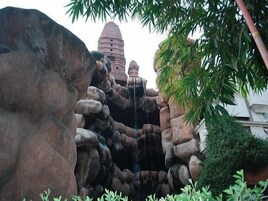 Formação rochosa com um elemento aquático e uma estrutura semelhante a um templo ao fundo.
