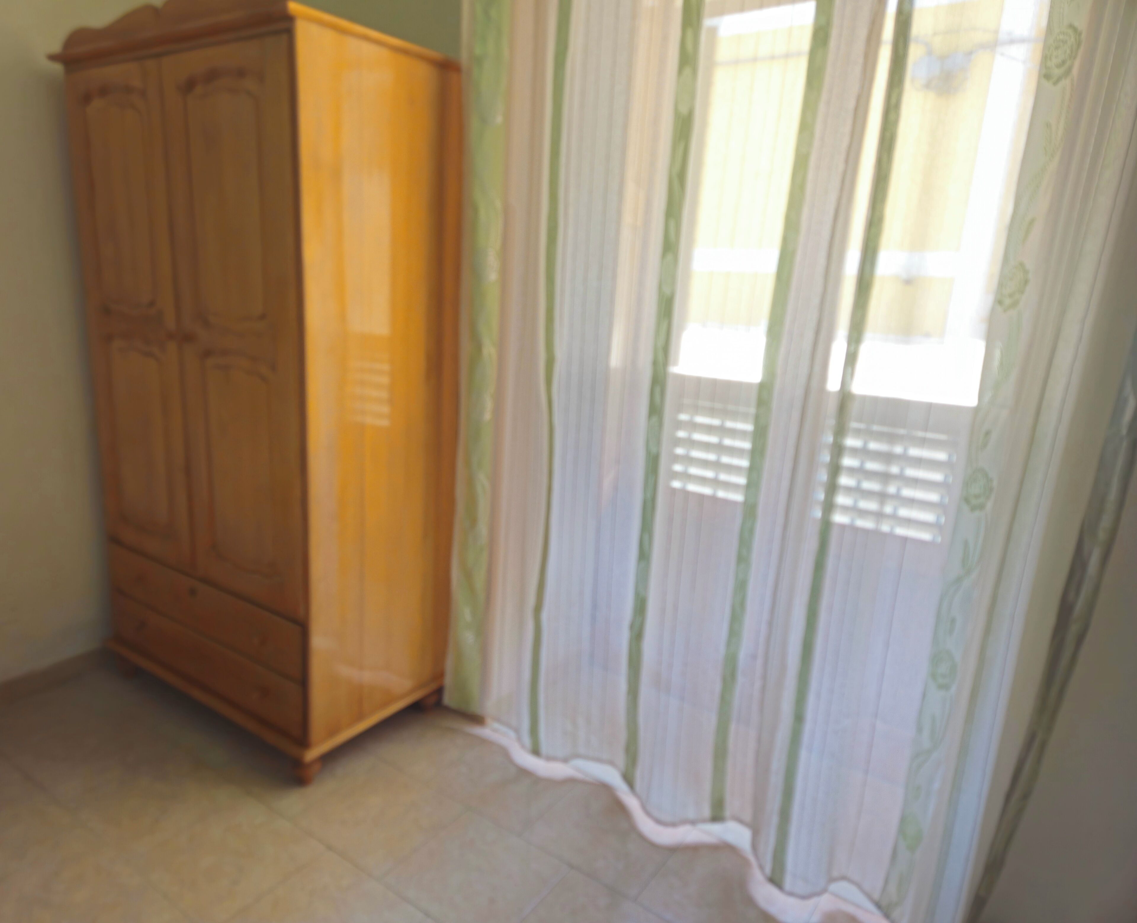 Quarto com guarda-roupa de madeira e janela com cortina listrada em verde e branco.