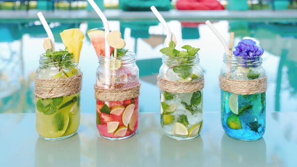Quatro potes de vidro com bebidas sobre uma mesa à beira da piscina.