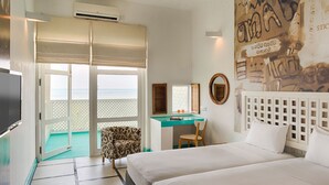 Quarto de hotel com duas camas, uma escrivaninha, uma cadeira, uma televisão e varanda com vista para o mar.