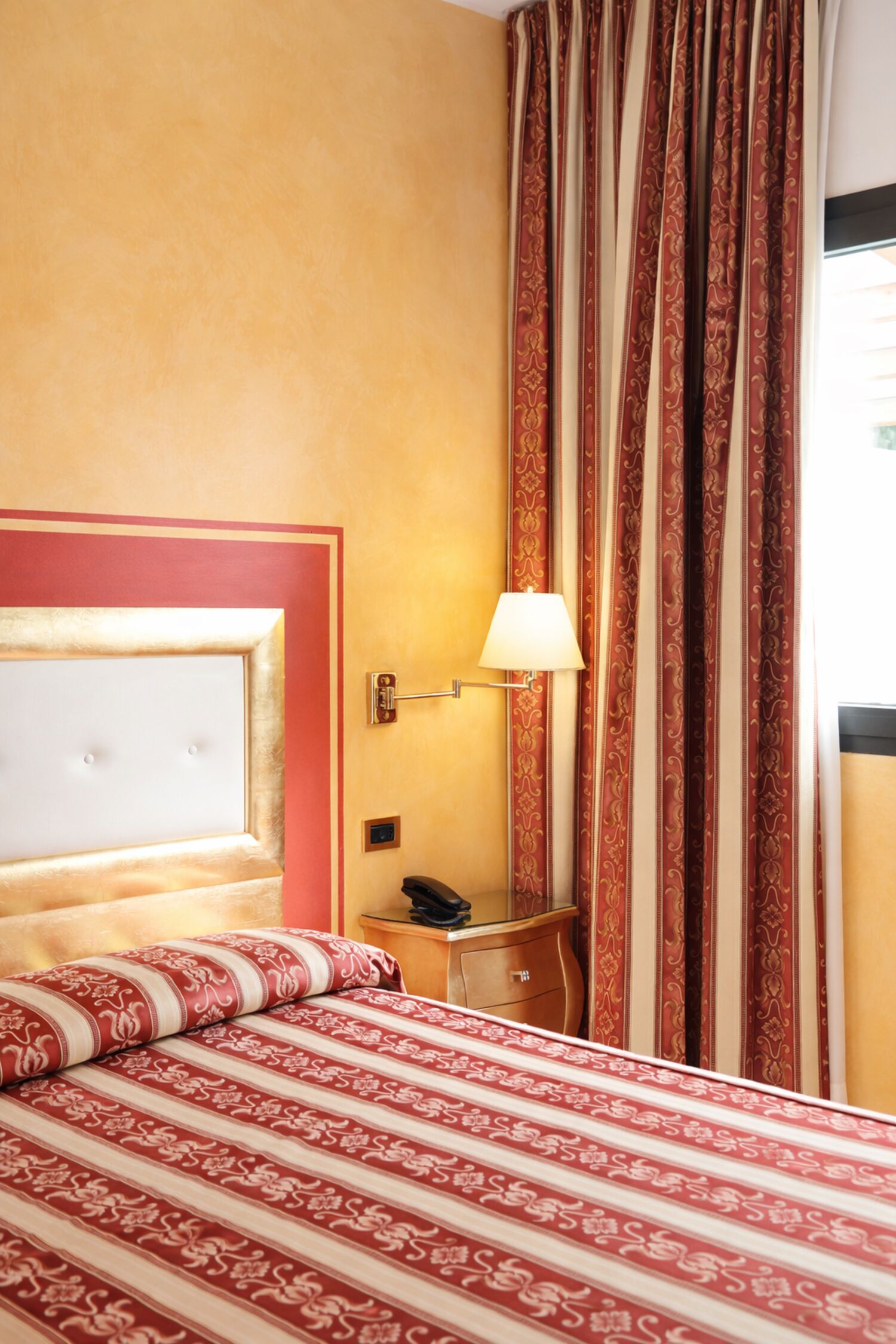 Quarto de hotel com uma cama, mesa de cabeceira, abajur e janela com cortinas.