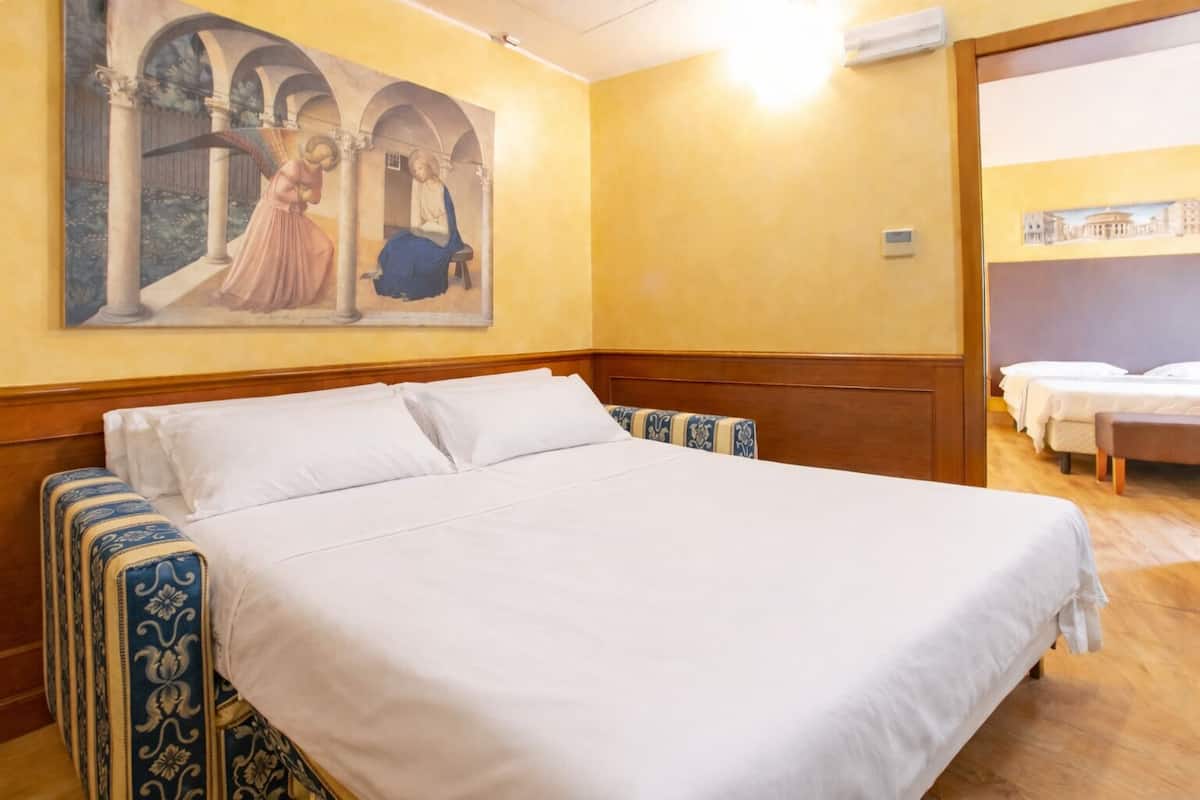 Quarto de hotel com uma cama grande, um quadro na parede e uma área de dormir separada.