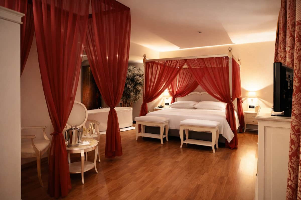 Um quarto espaçoso com uma cama grande, um espaço de estar com mesa e cadeiras, e uma televisão.