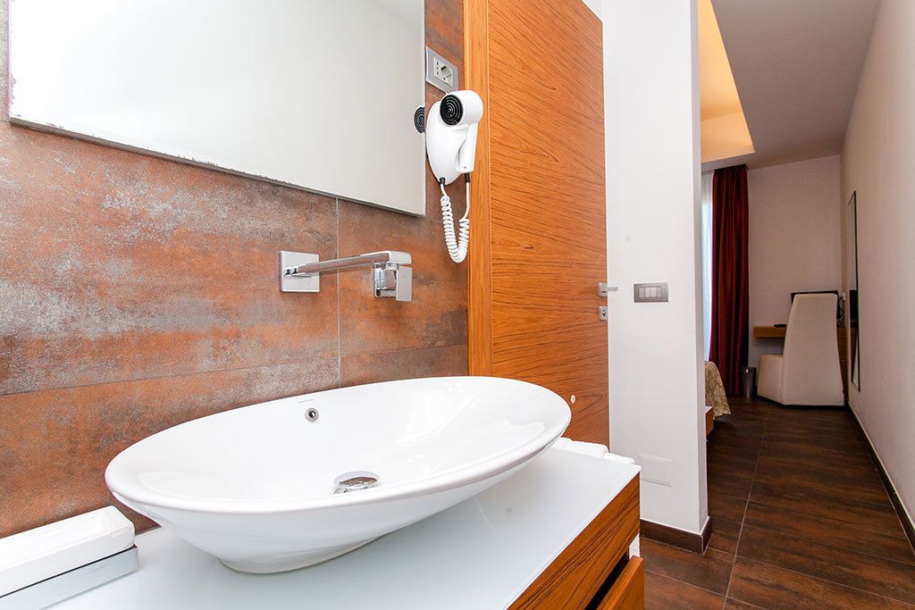 Um banheiro moderno com uma pia oval grande, um secador de cabelo fixado na parede e uma porta de madeira.