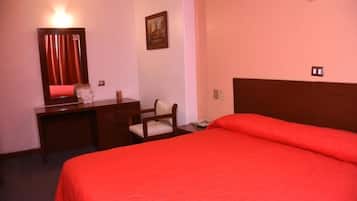 Quarto de hotel com uma cama grande, uma escrivaninha com cadeira, um espelho e uma luminária fixada na parede.