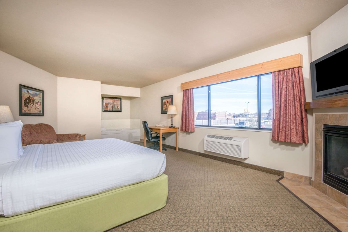 Quarto de hotel com cama, escrivaninha, cadeira e uma janela grande com vista.