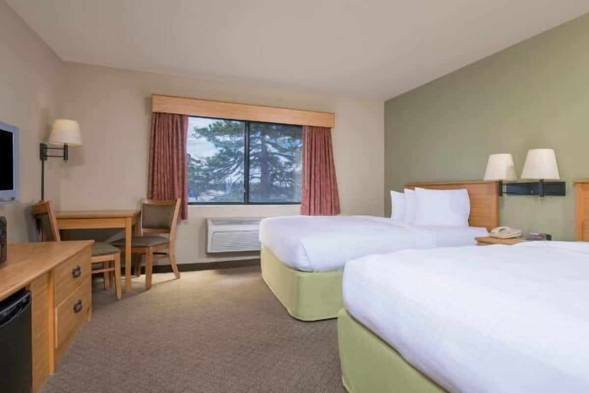 Quarto de hotel com duas camas, uma escrivaninha, uma cadeira, uma televisão e uma janela com cortinas.