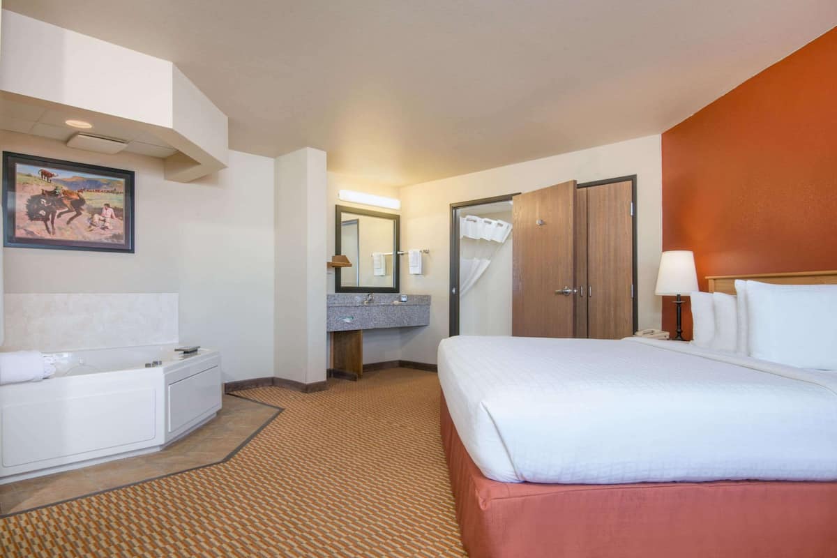 Quarto de hotel com uma cama, banheiro com pia e espelho, e um quadro na parede.
