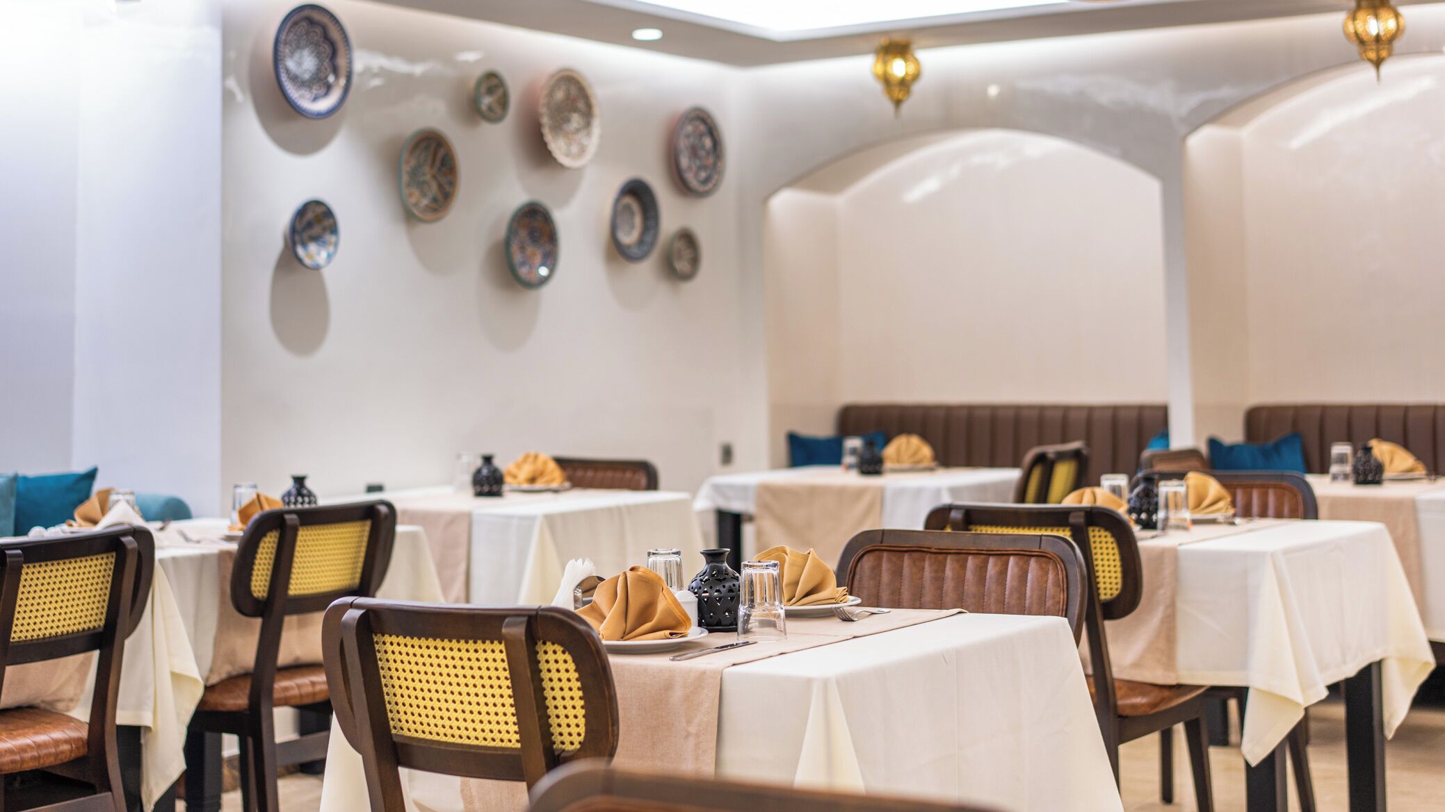 Restaurante com mesas redondas, cadeiras e uma parede decorada com pratos.