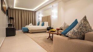 Quarto de hotel moderno com cama, sofá e uma pequena mesa com frutas.