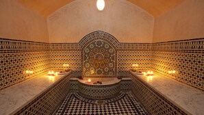 Um banho tradicional marroquino com azulejos elaborados e uma fonte central.