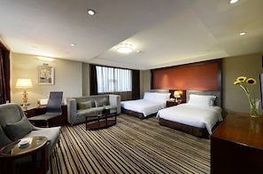 Quarto de hotel com duas camas, um sofá, uma mesa e uma cadeira.