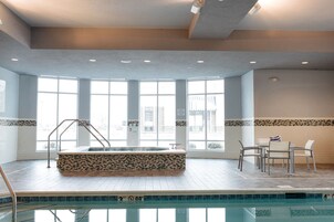 Piscina interna com hidromassagem, grandes janelas e área de estar com cadeiras e mesa.