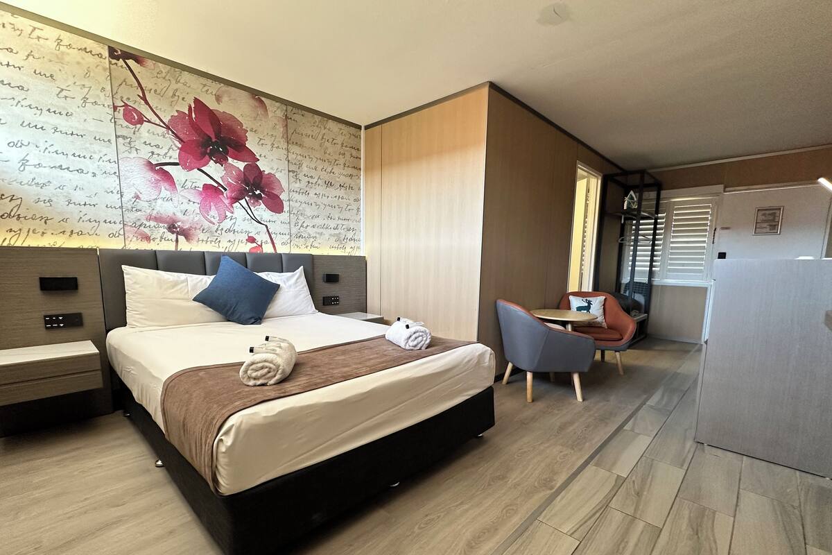 Quarto de hotel moderno com uma cama grande, mesas de cabeceira, escrivaninha e uma cadeira.