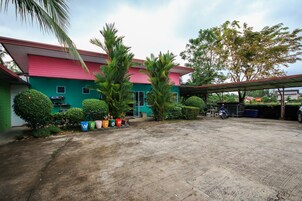 Uma área externa ampla com piso de concreto, cercada por vegetação e um edifício colorido com telhado vermelho.