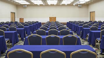 Sala de conferência com fileiras de mesas e cadeiras, um púlpito e uma tela de projeção.