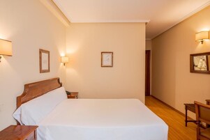 Quarto de hotel com uma cama de solteiro, mesas de cabeceira, luminárias fixadas na parede e quadros emoldurados.