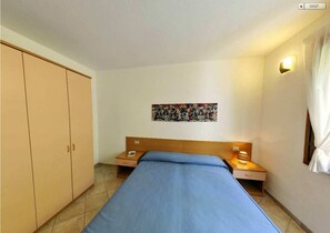 Quarto com cama, guarda-roupa, mesa de cabeceira e luminária na parede.