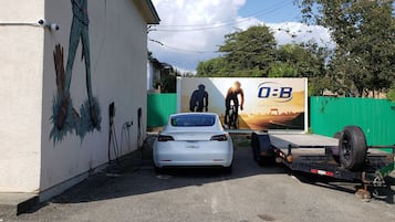 Um carro branco estacionado ao lado de uma cerca verde, com um outdoor ao fundo publicando Oak Bay Bicycles.