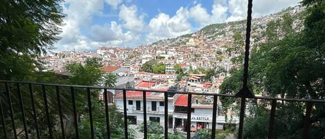 Uma varanda com vista para uma cidade em encosta, com uma mistura de edifícios residenciais e comerciais, e uma igreja com uma torre de sino em destaque.