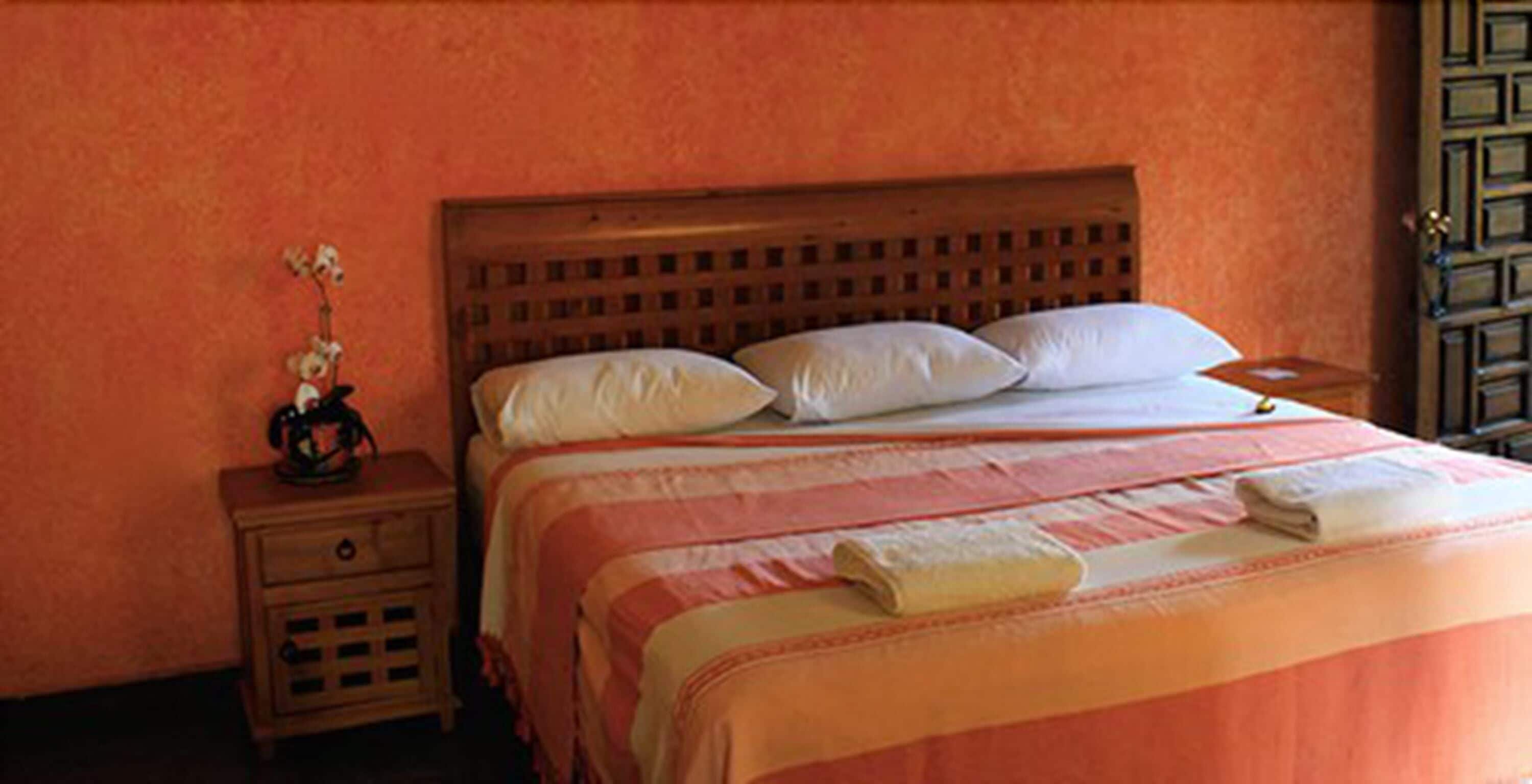 Quarto com cabeceira de madeira, mesa de cabeceira com abajur e cama com almofadas e cobertor.
