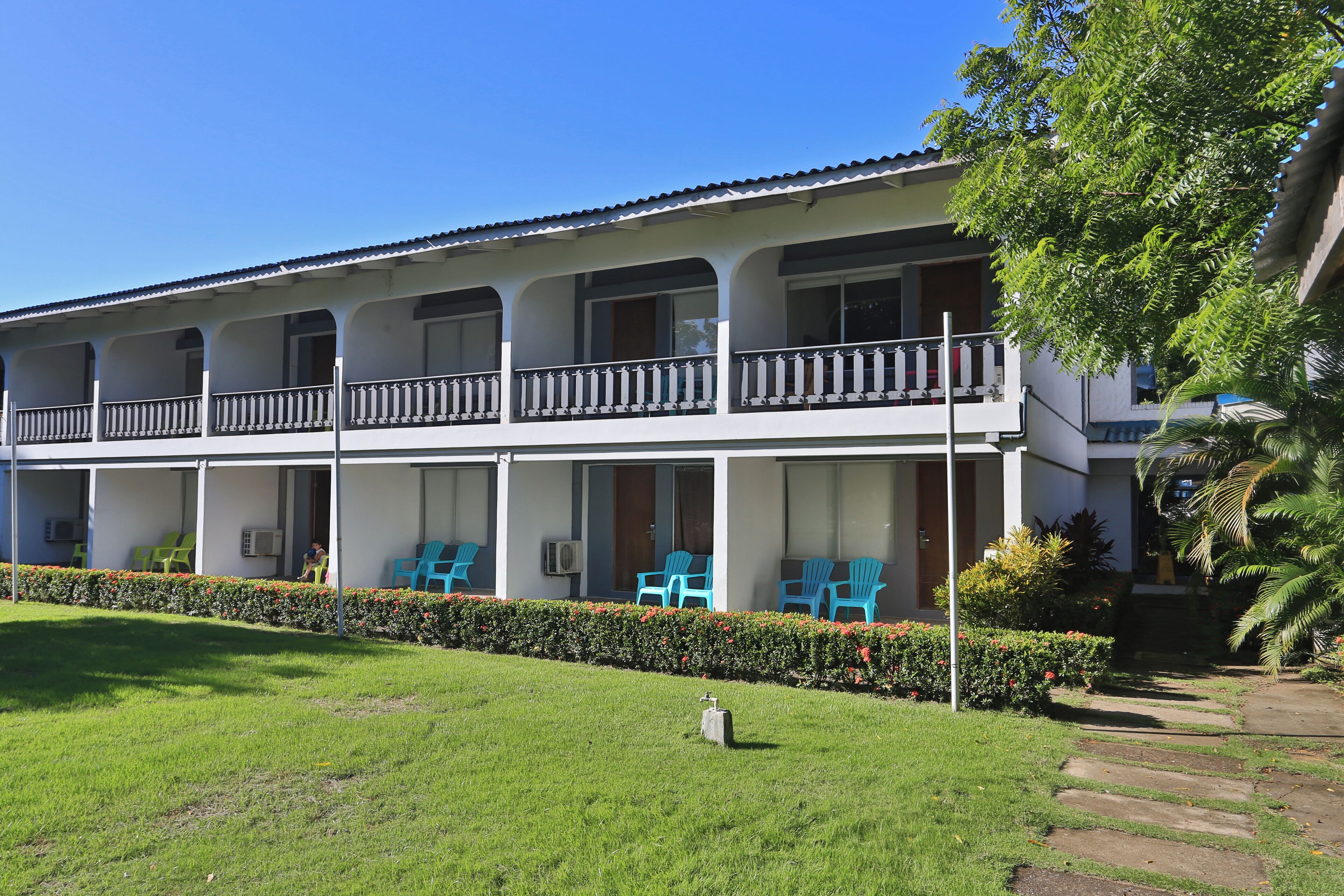 Um edifício de dois andares com varanda, área de estar externa e gramado bem cuidado.