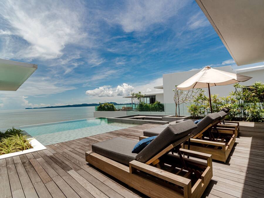 Um deck de madeira com cadeiras de descanso e piscina com vista para a água.