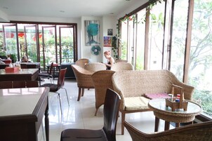 Um quarto amplo com móveis de vime, janelas grandes e um ventilador.