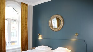 Quarto com cama, mesa de cabeceira, espelho e janela com cortinas.