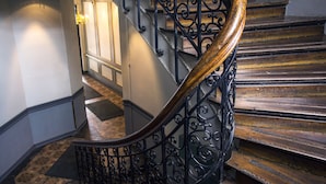 Uma escadaria de madeira com grades de metal preto detalhadas e um corrimão de madeira polida.