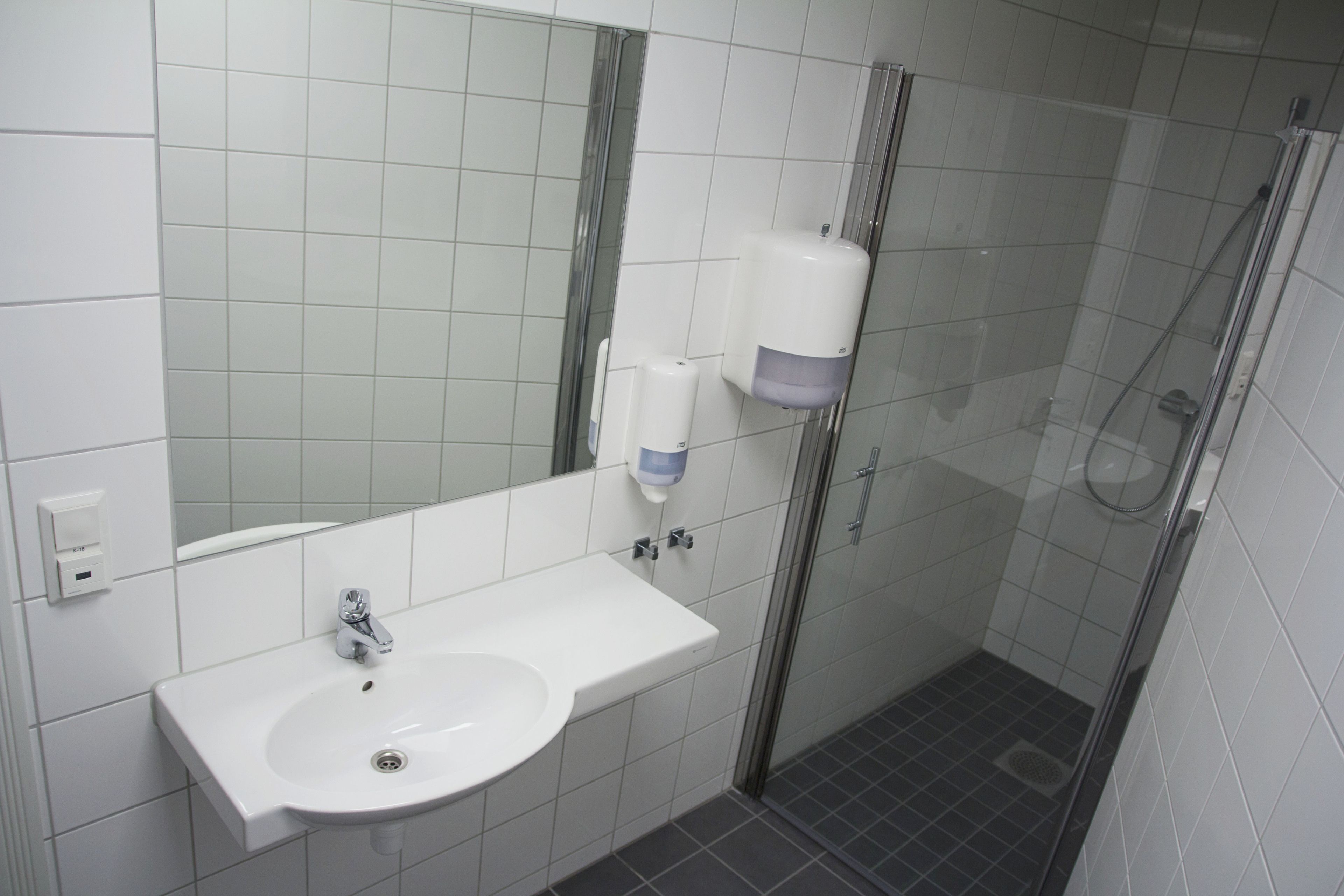 Casa de banho com lavatório branco, espelho, dispensador de sabonete líquido e cabine de duche em vidro.