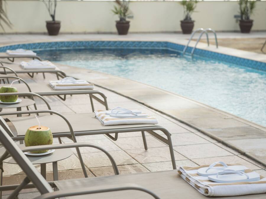 Uma área à beira da piscina com espreguiçadeiras, uma piscina pequena e plantas em vasos.
