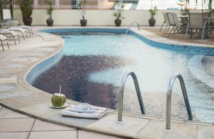 Piscina com duas escadas de metal, uma bebida de coco e uma toalha na borda.