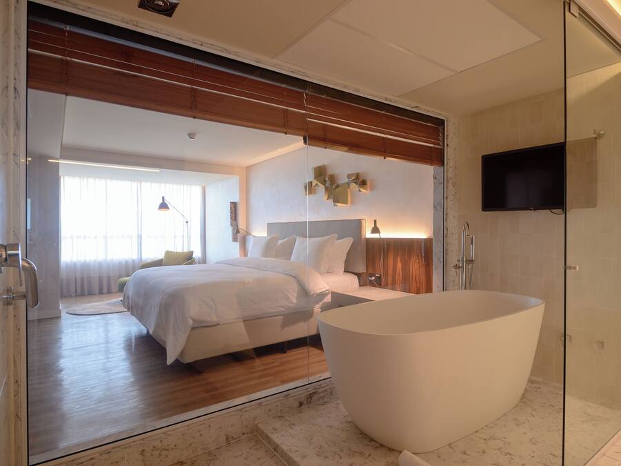 Quarto moderno com cama grande, box de vidro para o chuveiro e uma banheira espaçosa.