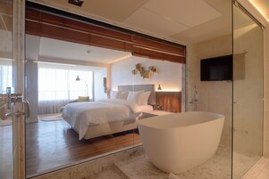 Quarto moderno com cama grande, box de vidro para o chuveiro e uma banheira espaçosa.