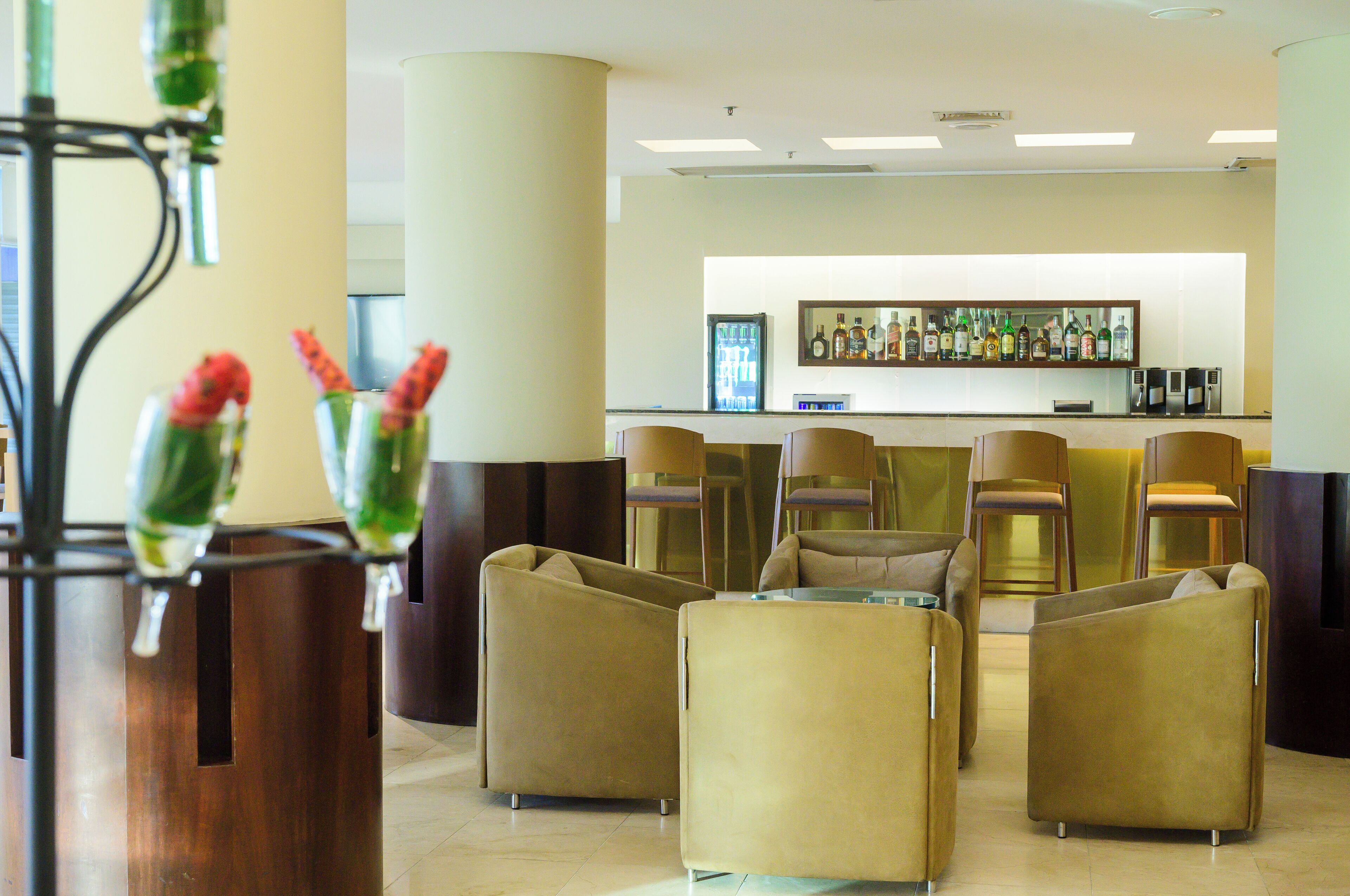 Um lobby com área de bar, opções de assentos e exposição de garrafas de bebidas.