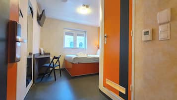 Quarto de hotel com cama, escrivaninha, cadeira e janela.