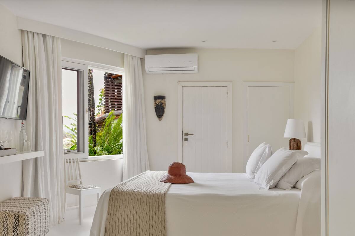 Um quarto com cama, televisão, janela com cortinas, porta e ar condicionado.