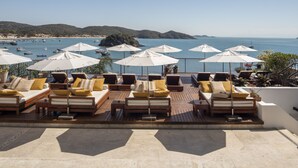 Um terraço com espreguiçadeiras e guarda-sóis com vista para um corpo de água e barcos.