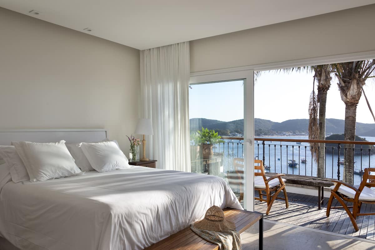 Quarto com uma cama grande, varanda com vista para o mar e área de jantar com mobiliário de madeira.