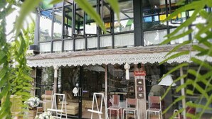 Um café acolhedor com mesas ao ar livre, um toldo rendado e vista para a rua.