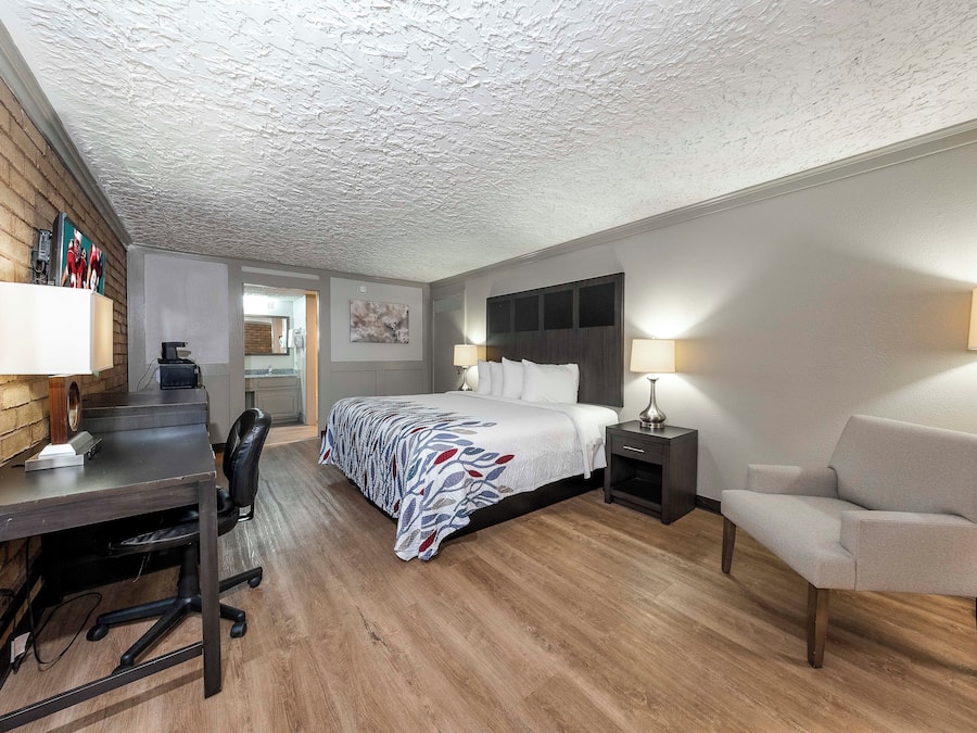 Quarto de hotel com cama, escrivaninha, cadeira e uma pequena cozinha.