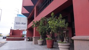Um hotel chamado Son-Mar, com fachada vermelha, plantas em vasos e uma placa indicando comodidades como restaurante, bar e internet WiFi.
