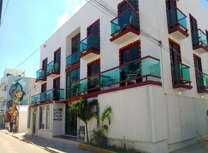 Um edifício com vários andares, varandas, um mural à esquerda e uma pequena área de estar externa.