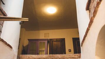 Uma escadaria com colunas brancas e um arco de tijolos que dá acesso a um quarto com uma porta e um aparelho de iluminação.