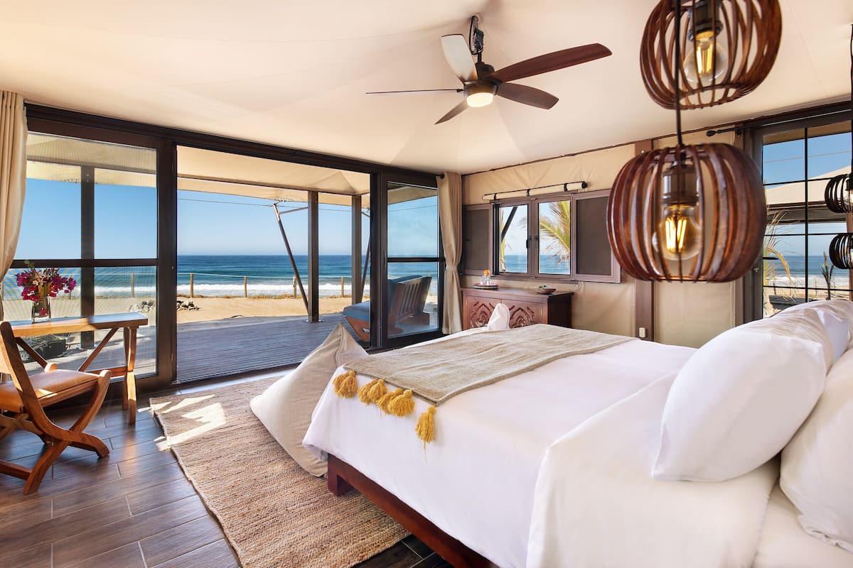 Quarto com uma cama grande, uma mesa e uma cadeira, com vista para uma praia.
