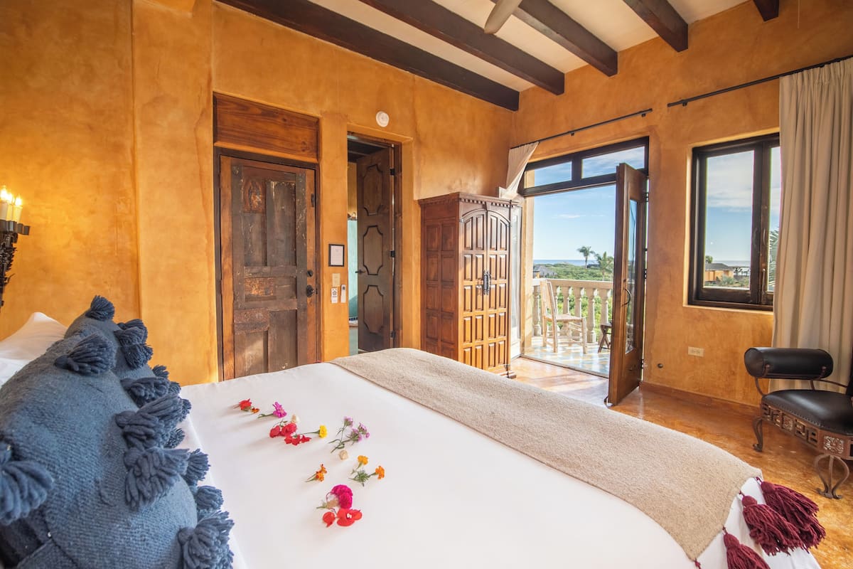 Quarto com uma cama grande, portas de madeira, uma varanda com vista e uma cadeira.